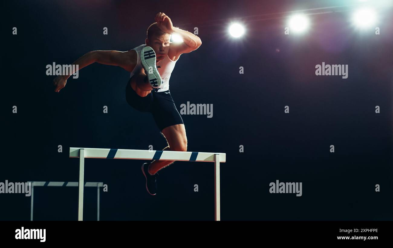 Male Athlete in Mid-air, Leaping Over Hurdle Under Bright Stadium ...