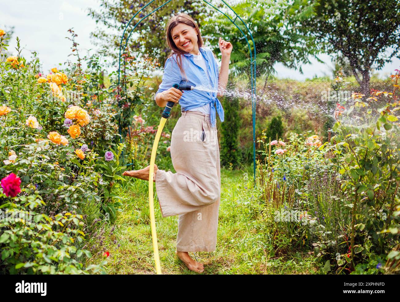 Happy woman gardener having fun watering plants with hose pipe in ...
