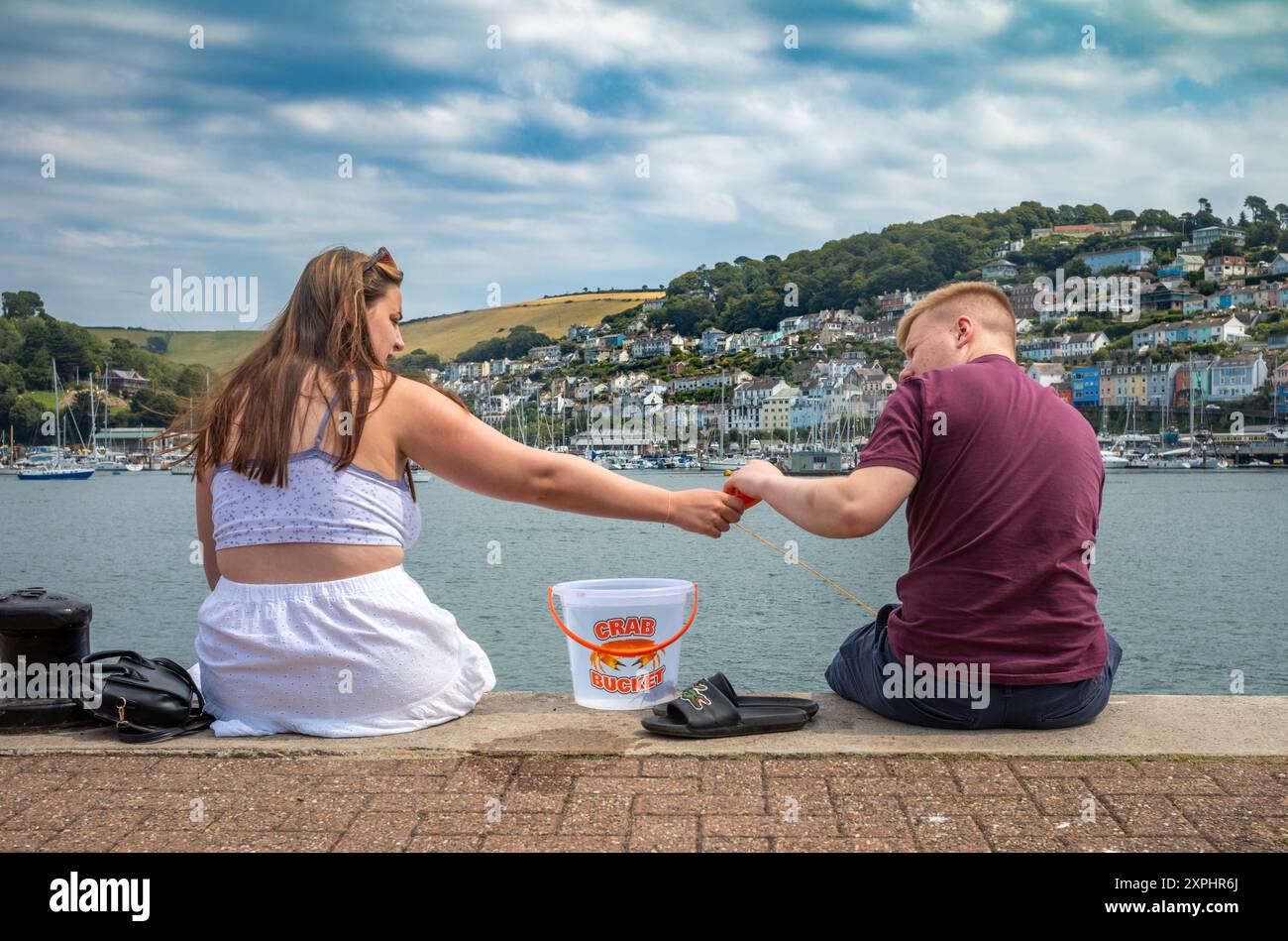 A young couple sit on the quayside crabbing as they try to catch crabs ...