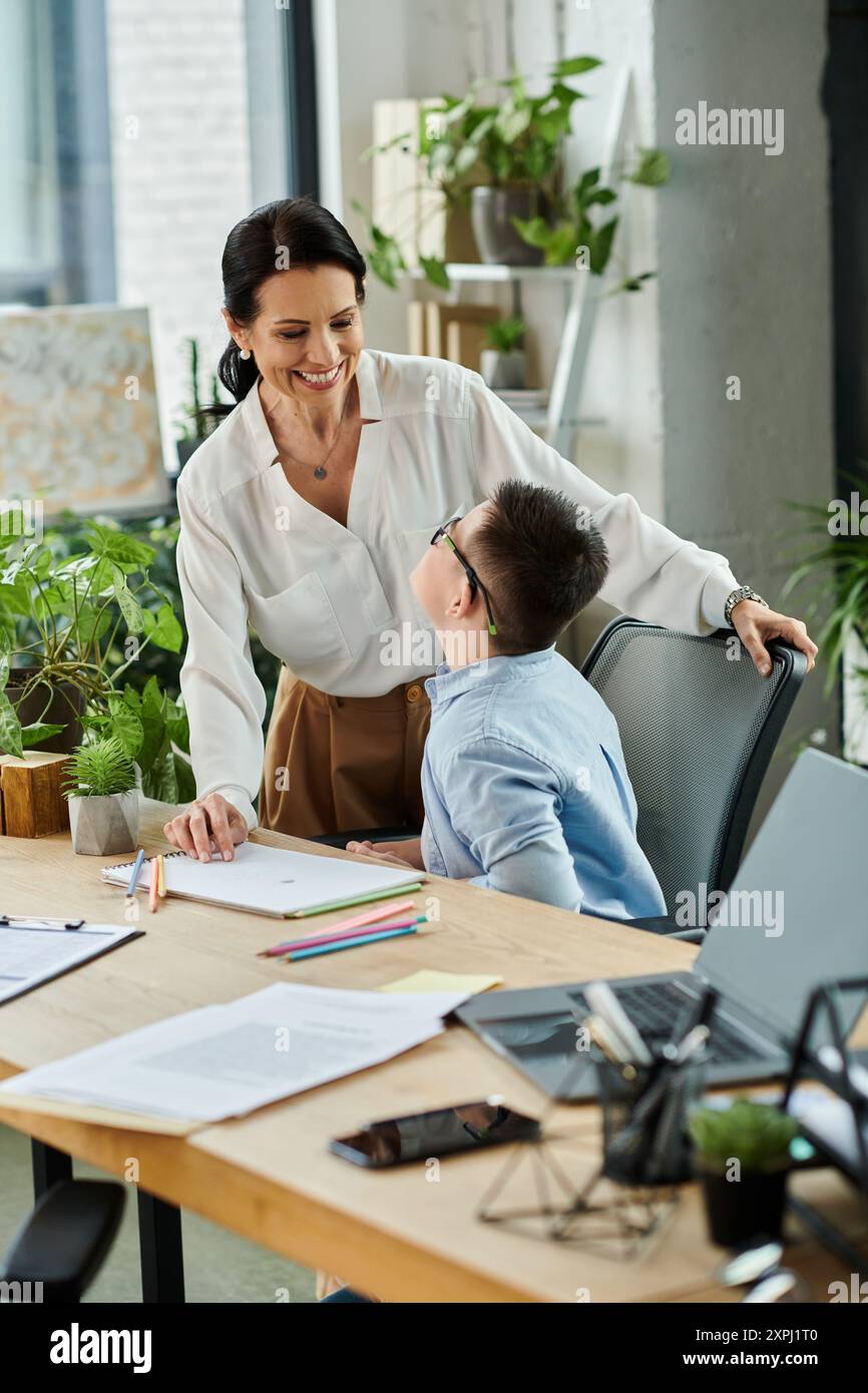 A mother smiles at her son while working at a desk in a modern office ...