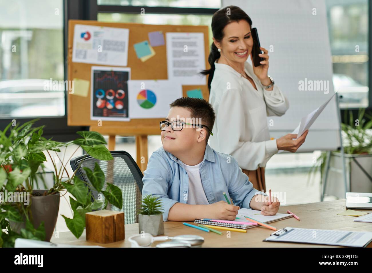 A mother works in an office, focused on a phone call, while her son ...