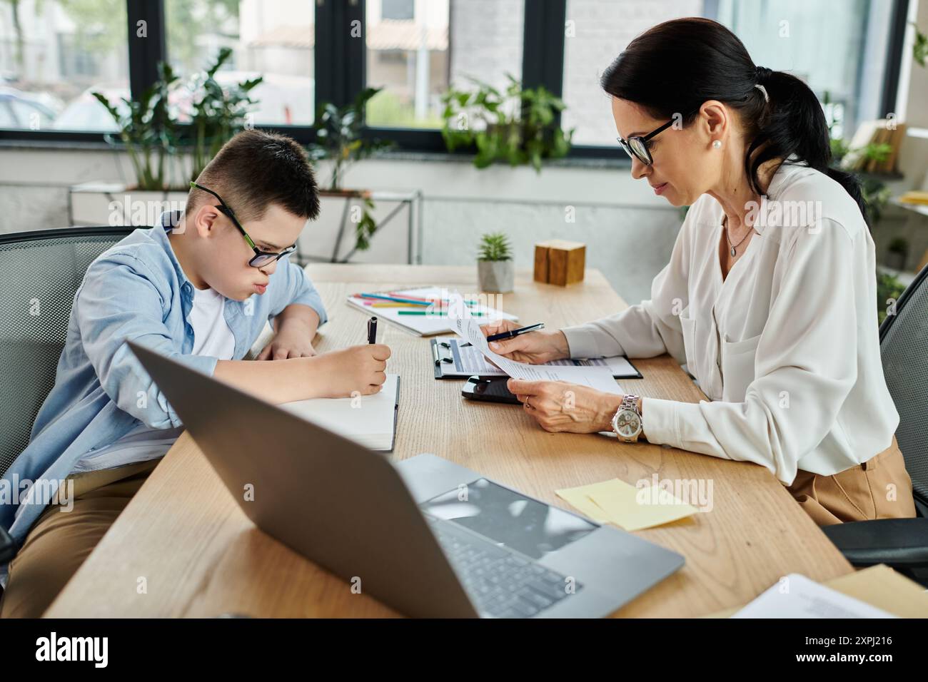A mother works on paperwork in the office while her son with Down ...
