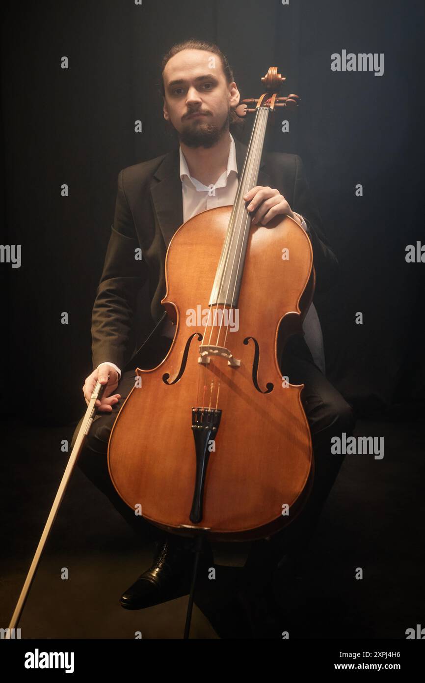 Vertical full shot of male classical music player holding cello while ...