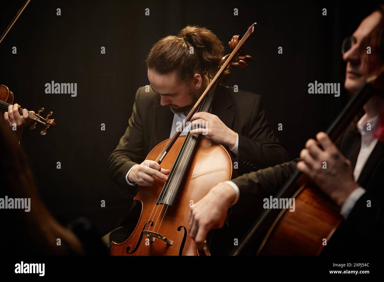 Medium shot of male musician looking down, while strumming cello ...