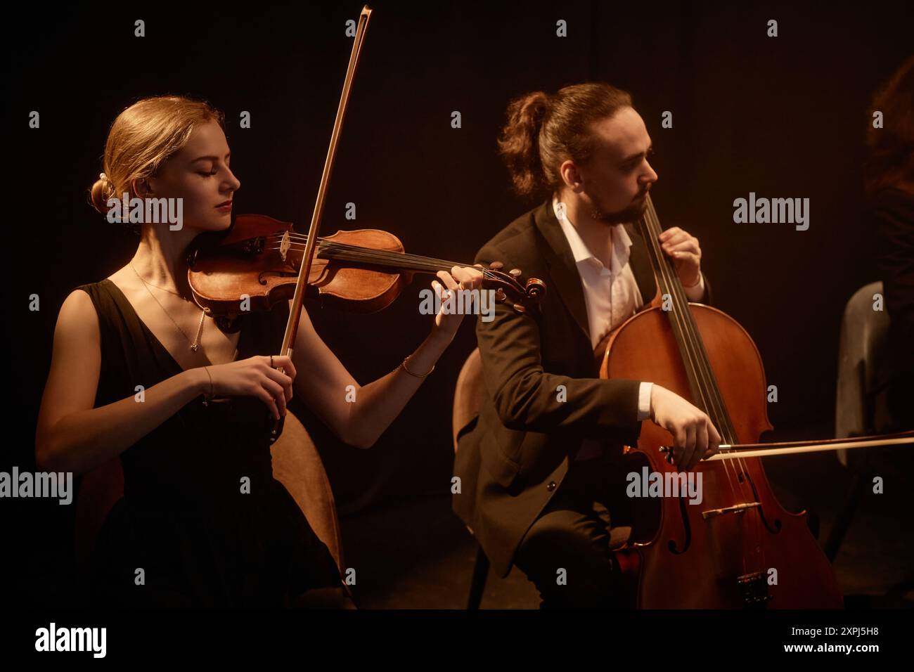 Side view of female and male classical music artists playing violin and ...