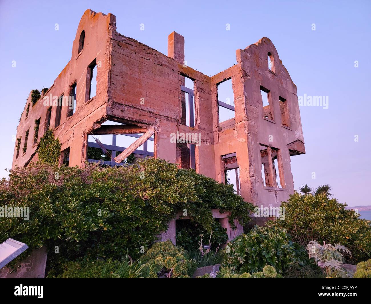 The ruins of Alcatraz Prison covered in greenery at sunset with a clear ...
