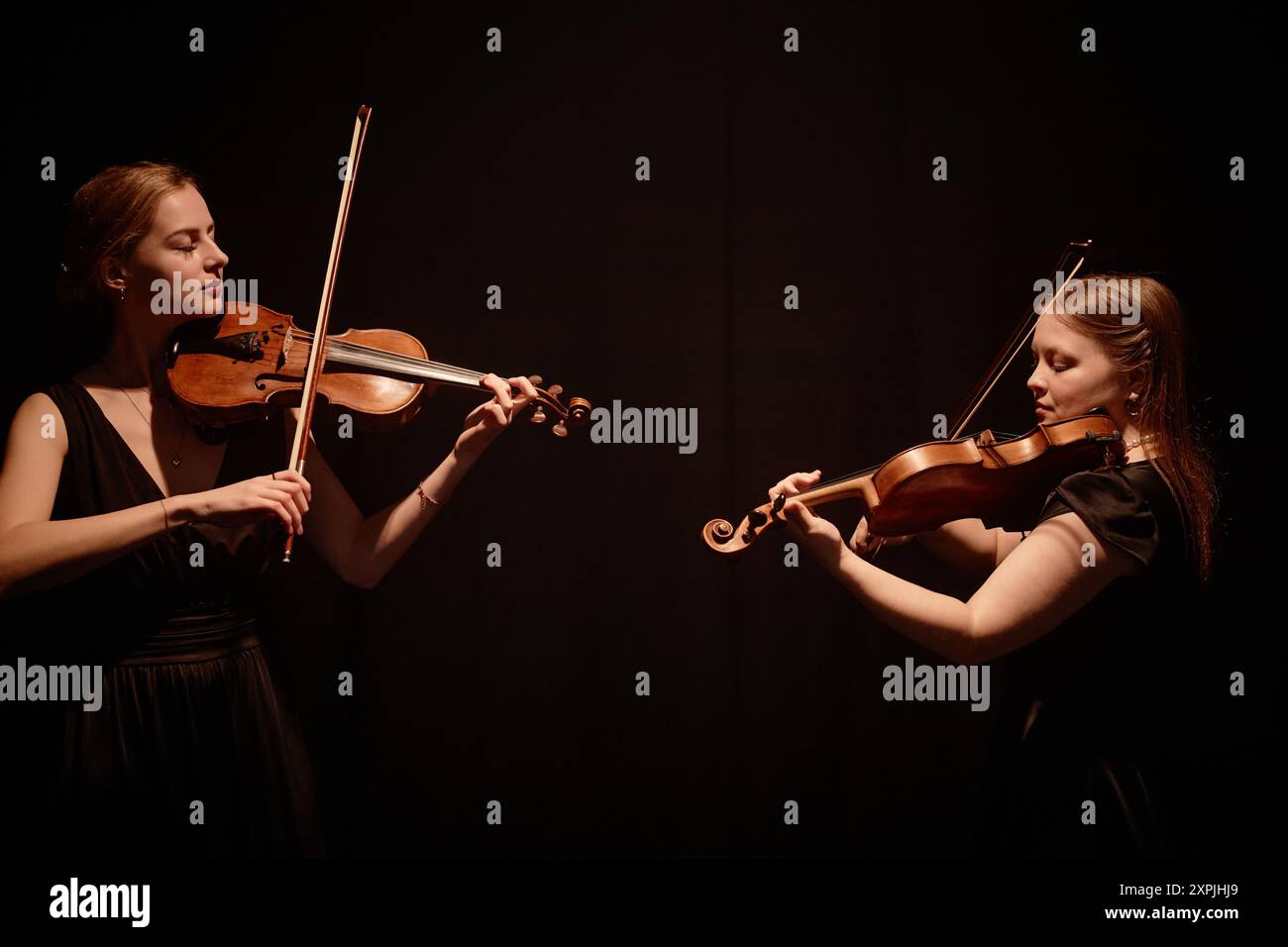 Side view of elegant string duet of female violinists playing classical ...