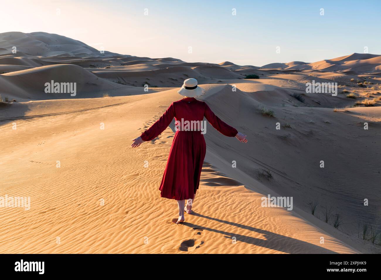 Woman walking in the desert sand dunes at sunset. traveler with arms up ...