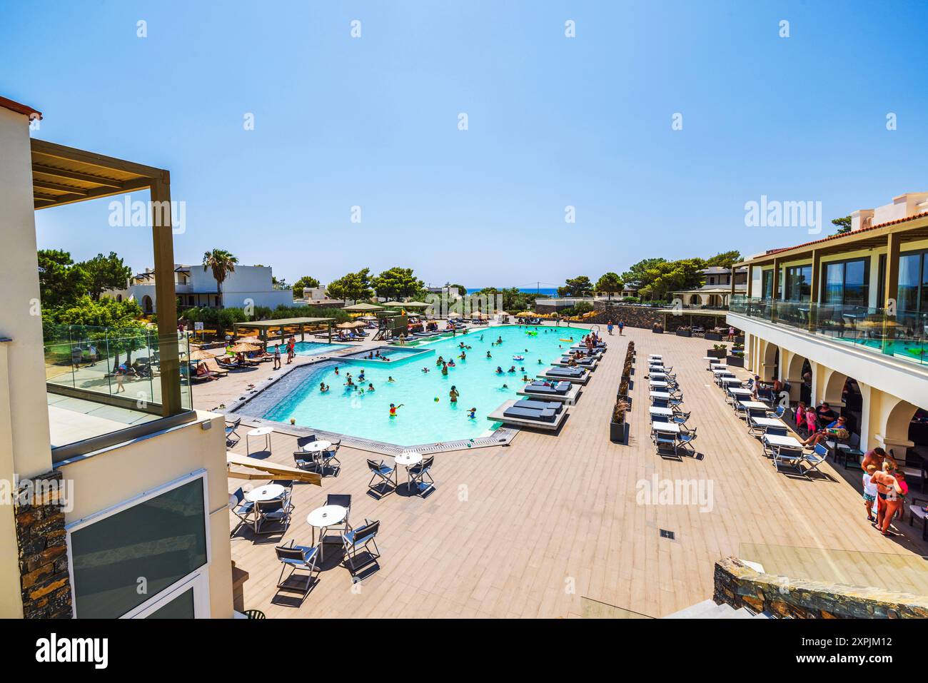 Hotel pool area with guests swimming and sunbathing, surrounded by sun ...