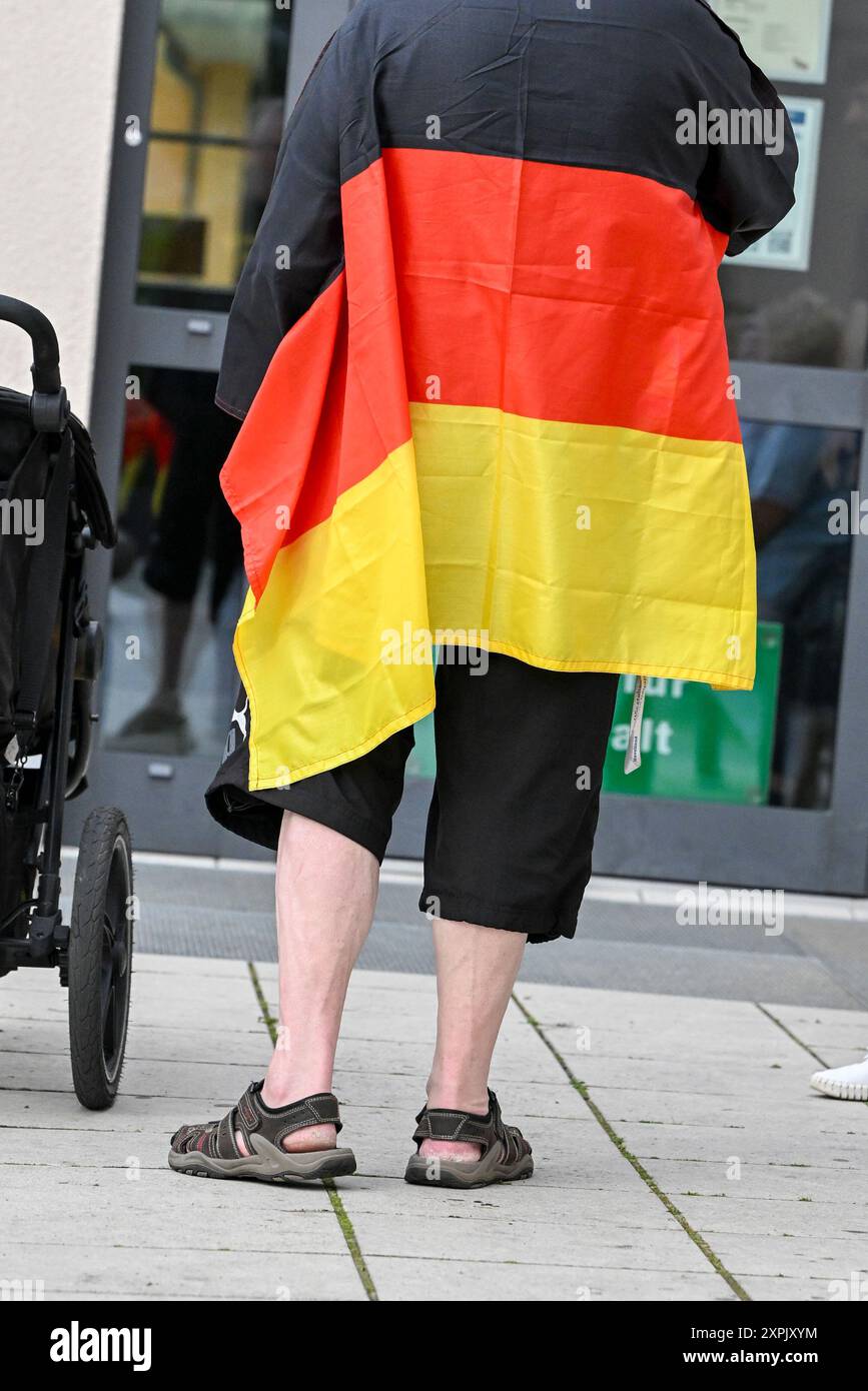 Falkensee, Germany. 31st July, 2024. A man with a German flag draped ...