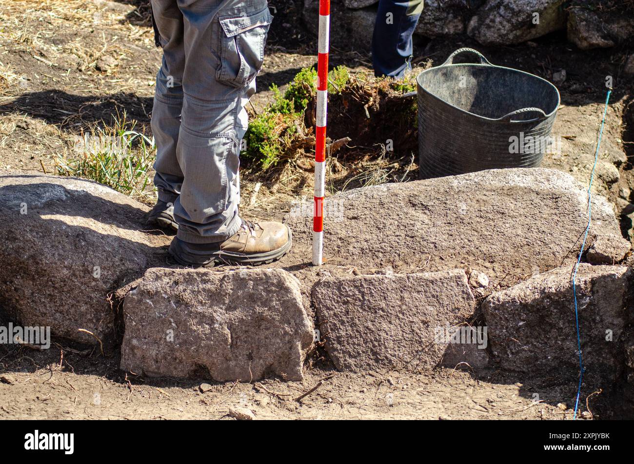 view of the legs of an archaeologist holding a range pole in an ...