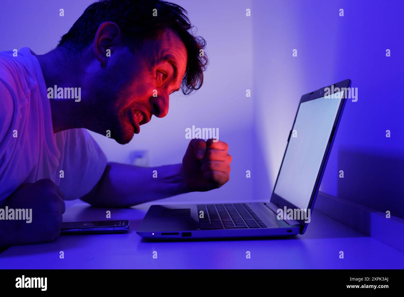 A man sits at a desk, intensely staring at a blank laptop screen, his ...