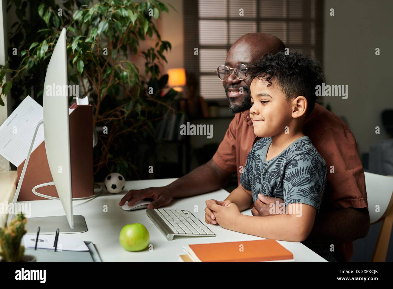 Happy cute little boy sitting by desk next to his father and both ...