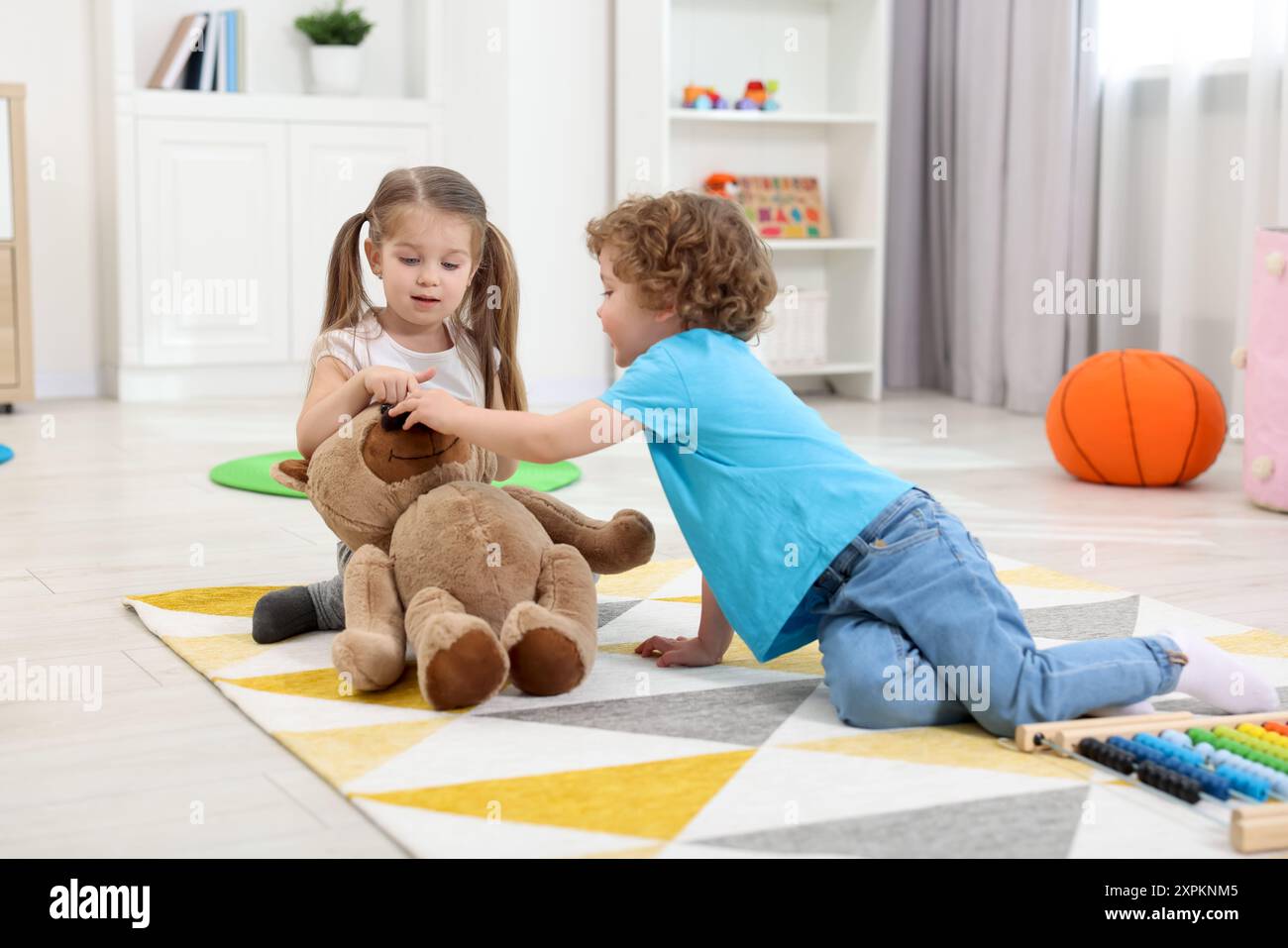 Cute little children playing with teddy bear on floor in kindergarten ...