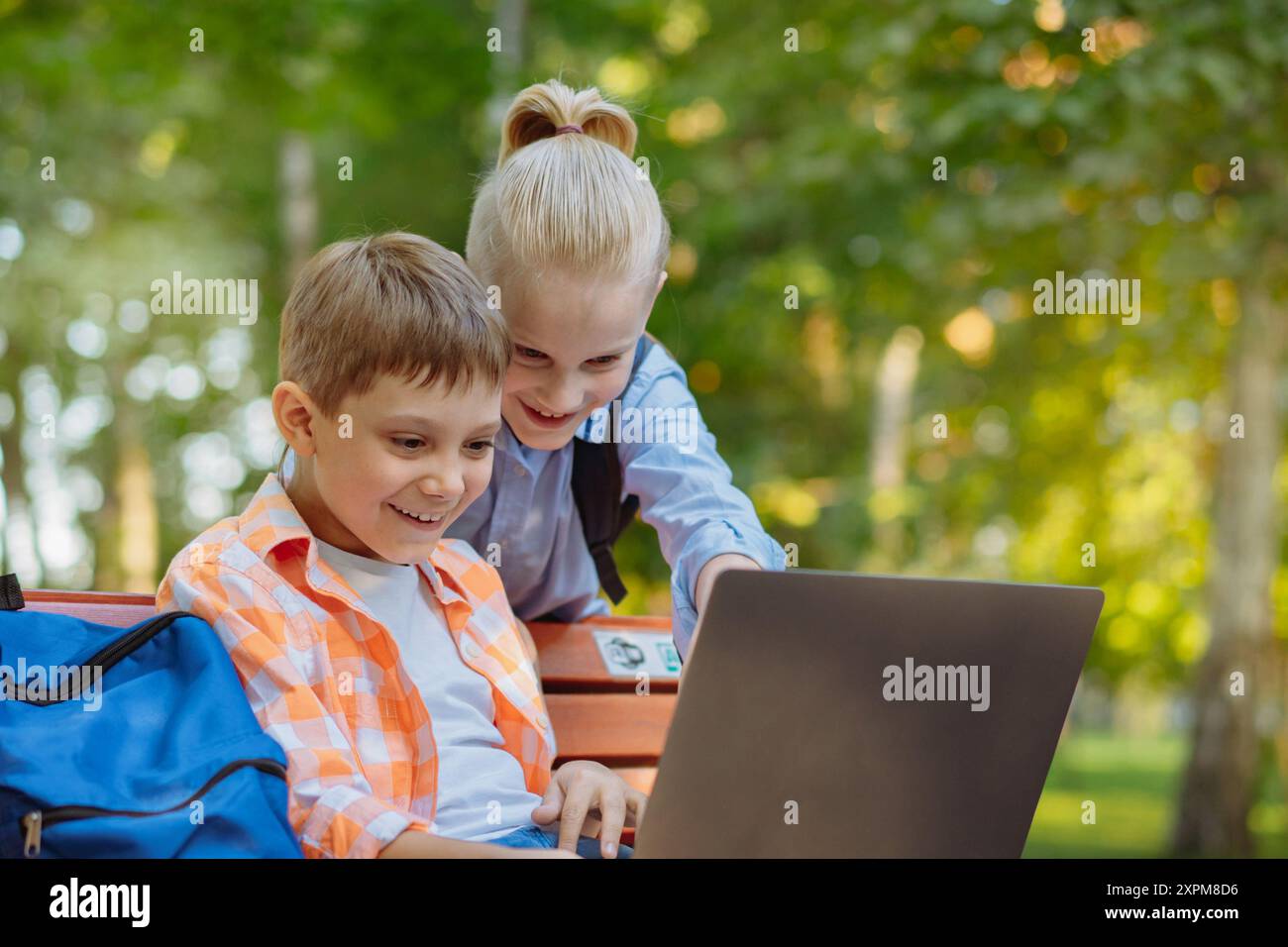 cute caucasian boys sitting on bench in park with laptop computer ...