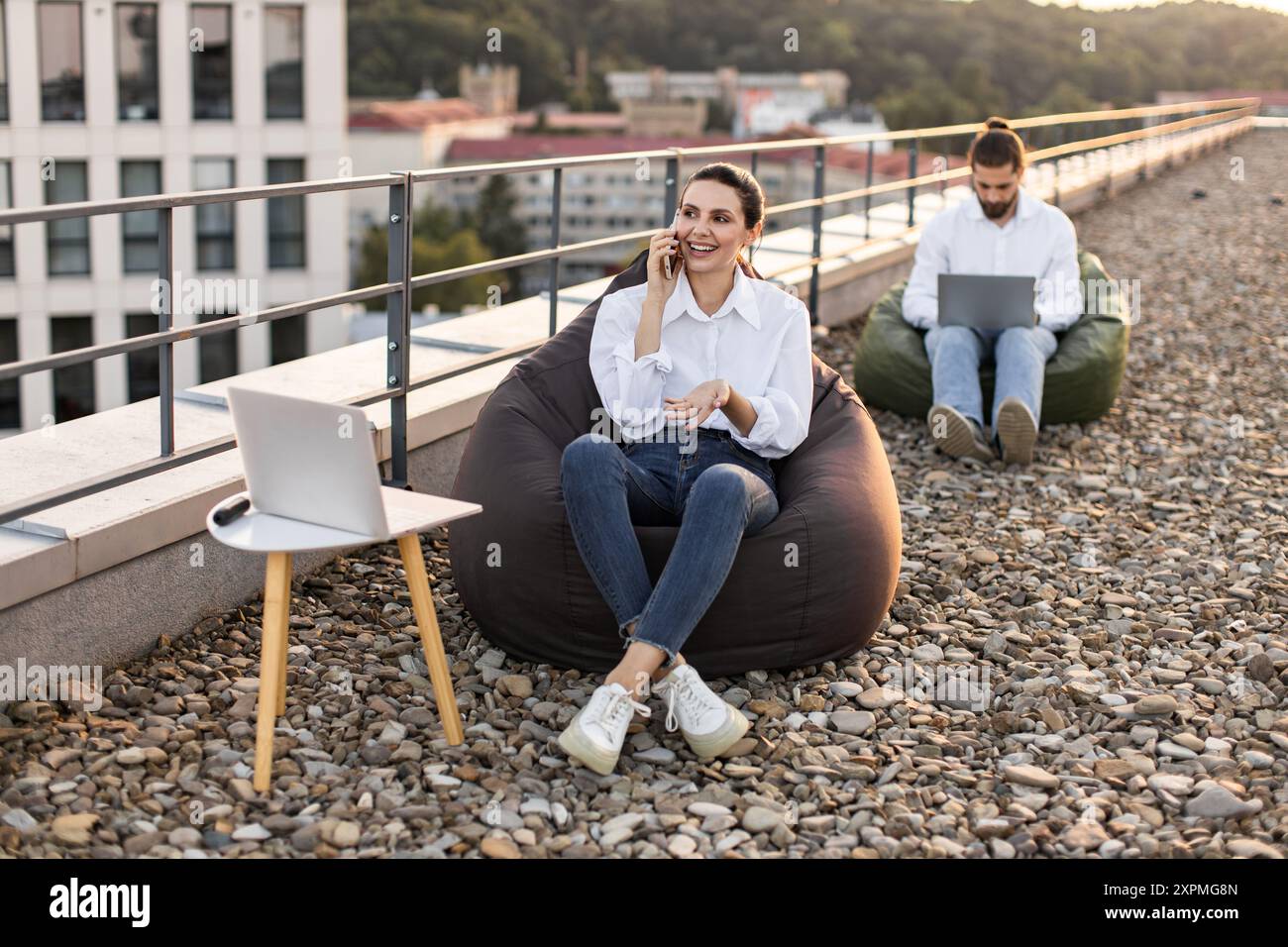 Two people working remotely on rooftop with laptops and bean bags Stock ...