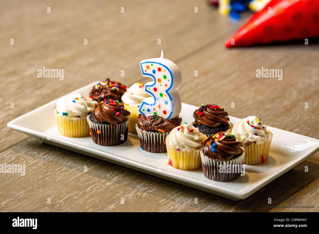 A close-up of festive cupcakes with a number 3 candle on a plate ...
