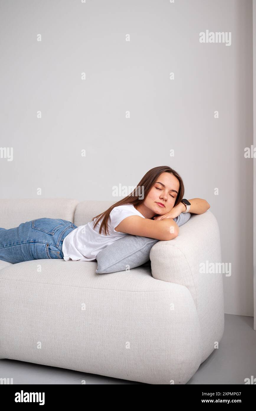 a beautiful slender girl lies on a light sofa and looks to the side ...