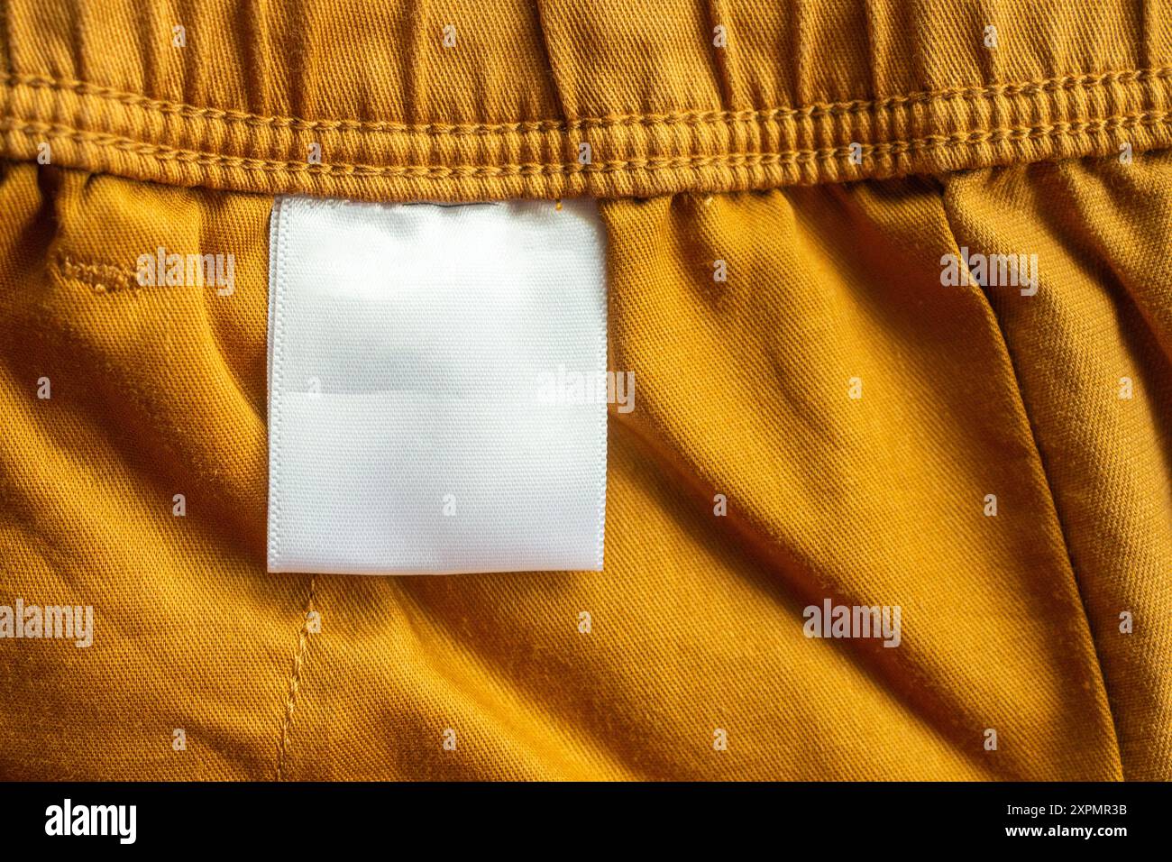 White blank clothing tag label on brown cotton shorts fabric texture ...