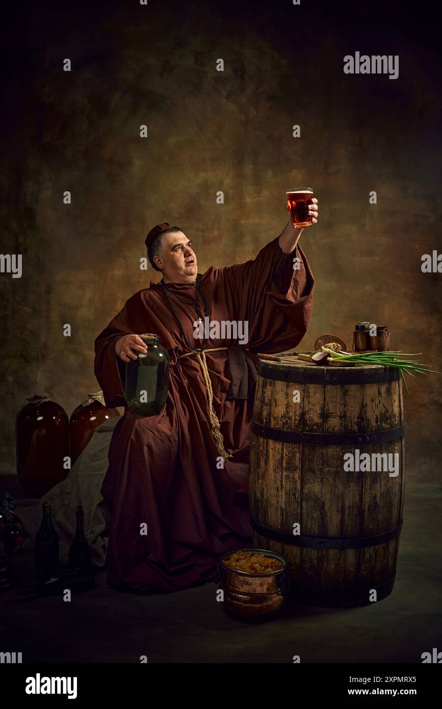 Man, medieval monk lifting glass of beer, pint of ale against dark ...