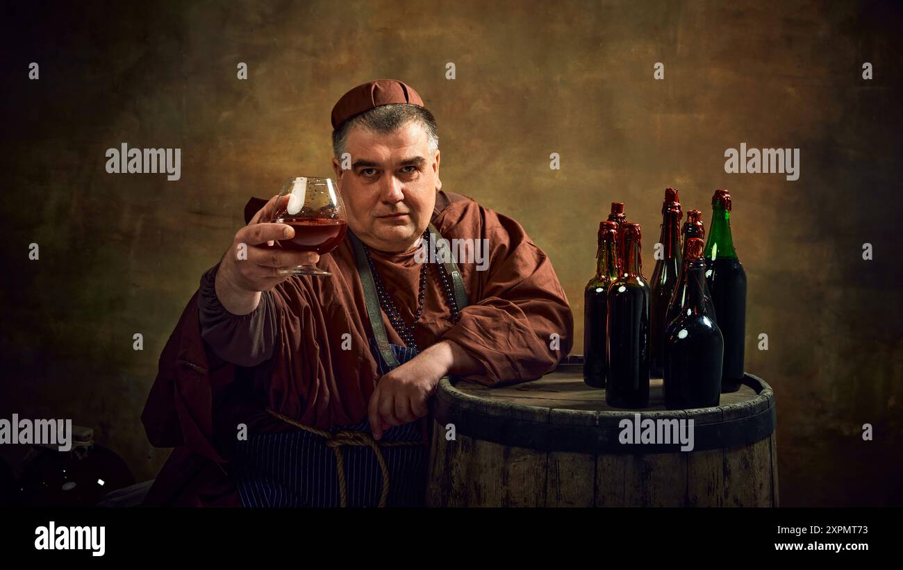 Man, medieval monk in robe raising glass filled with brown liquid, beer ...