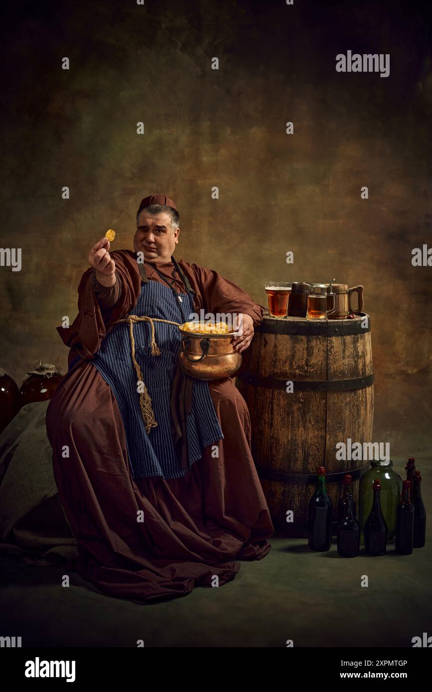 Man, monk in period attire sitting next to wooden barrel of beer, with ...