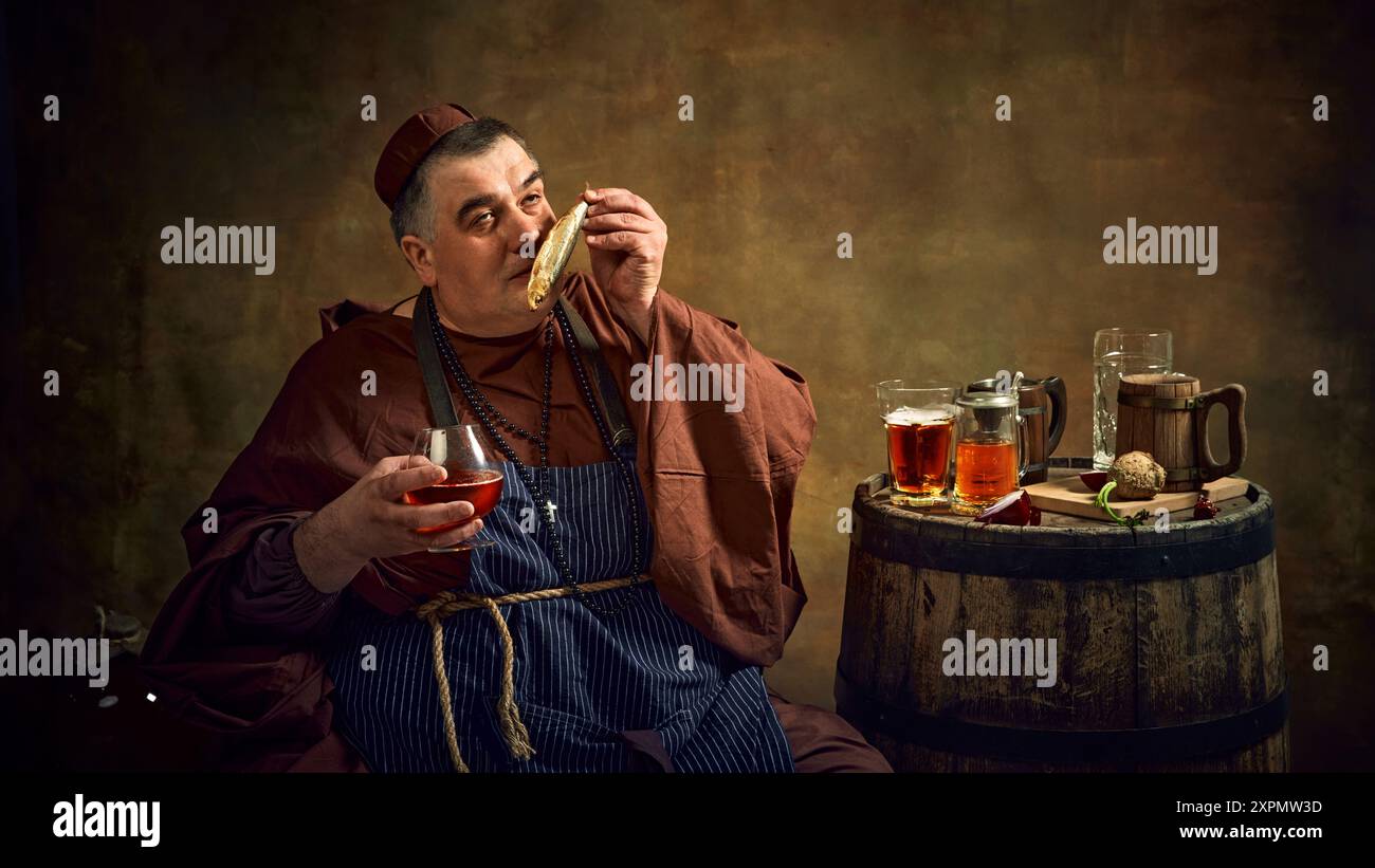 Man, monk sitting with glass of cognac, eating fish as appetizer ...