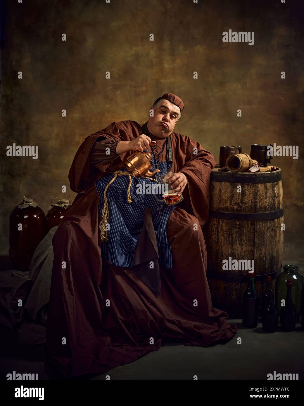Medieval monk in period clothes pouring beer into mug from kettle ...