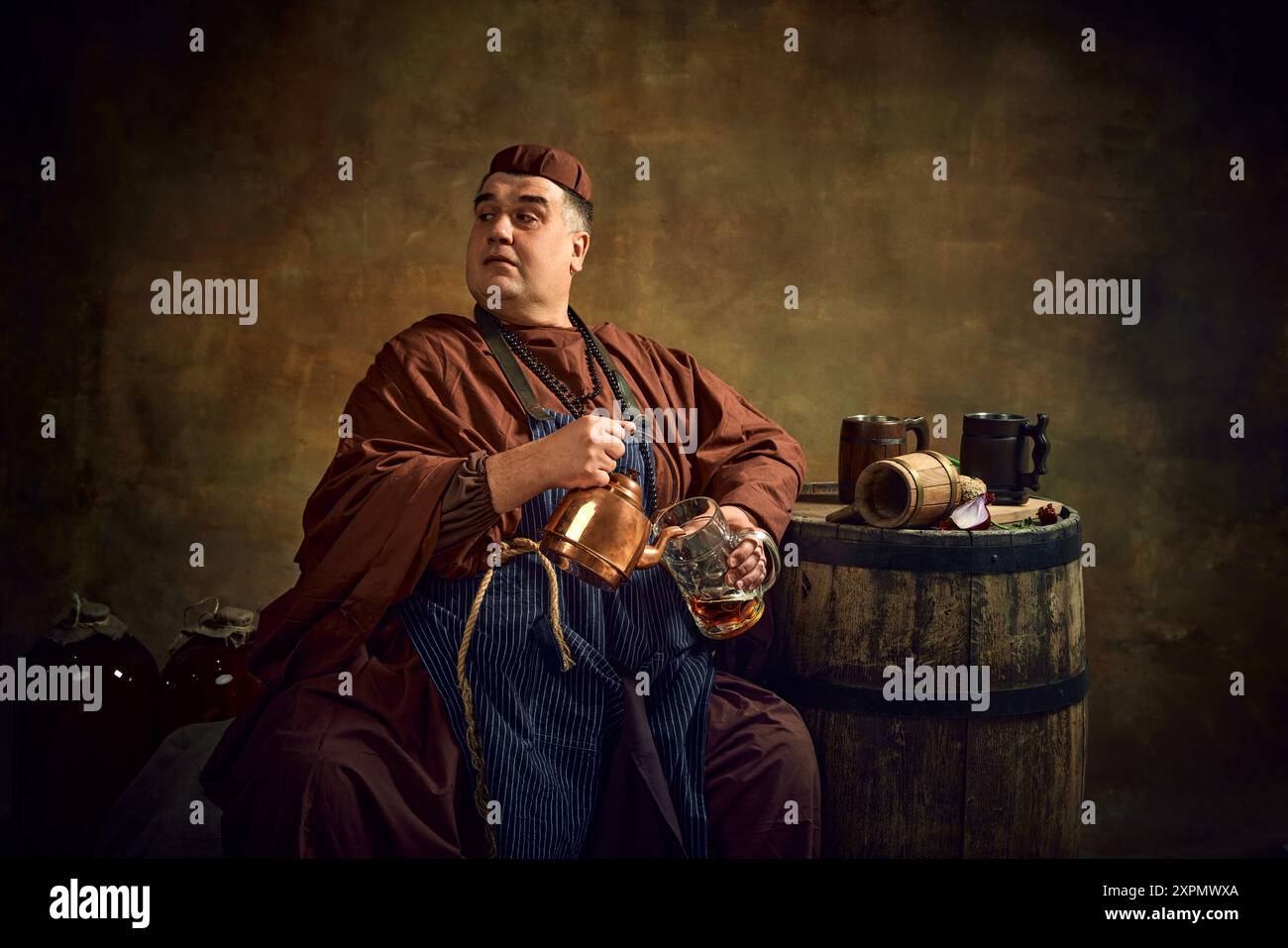 Medieval monk in period clothes pouring beer into mug from kettle ...