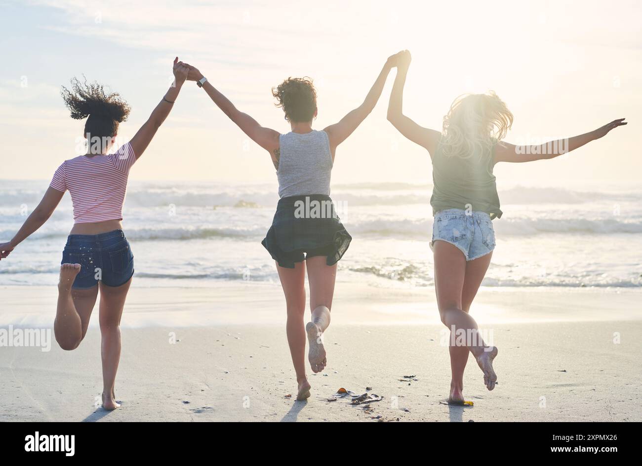 Back, group and women on beach for hands up, freedom and bonding ...