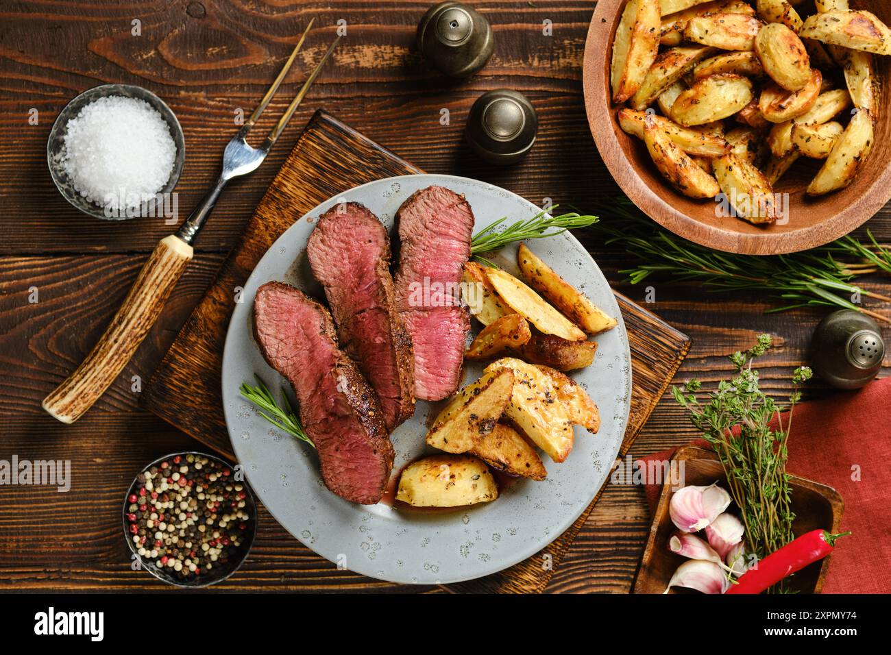 Overhead view of sliced beef steak with baked potato wedges and scented herbs on a plate Stock ...