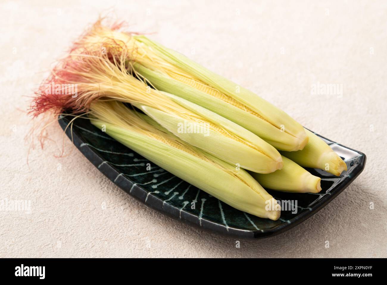 Raw, fresh baby corn in the husk with red silk in basket sieve plate on ...