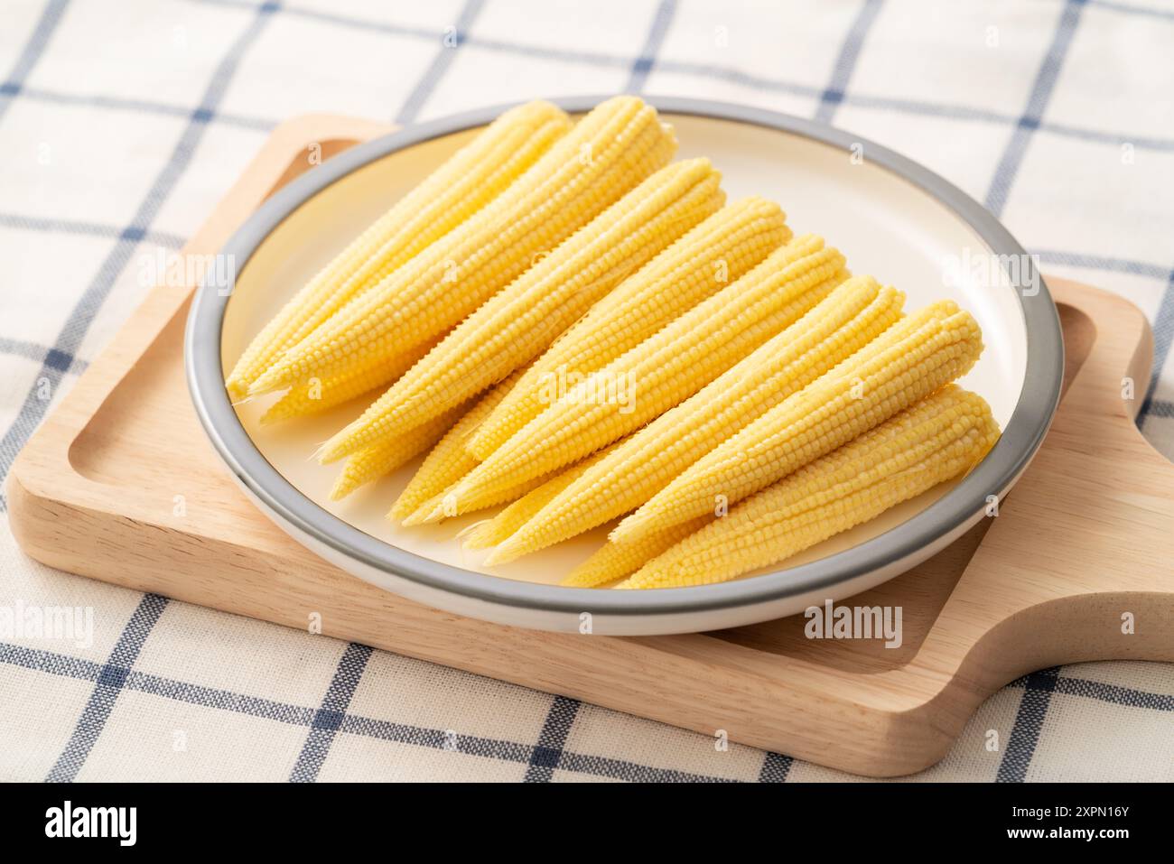 Raw, fresh baby corn in the husk with red silk in basket sieve plate on ...