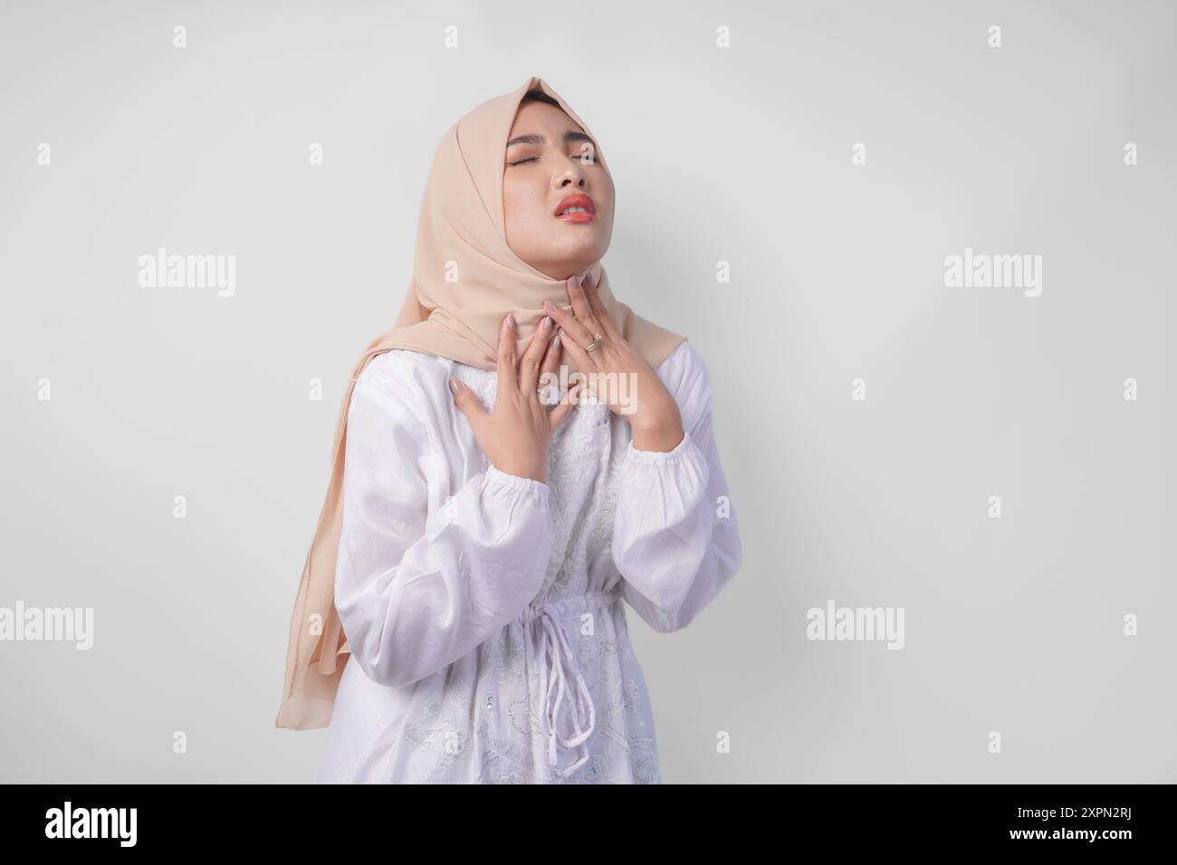 Tired Asian Muslim woman in white dress and hijab holding her neck ...