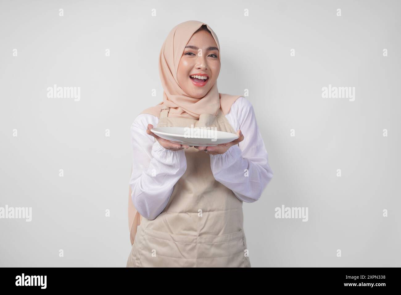 Beautiful young Asian Muslim woman in hijab and cream apron presenting ...