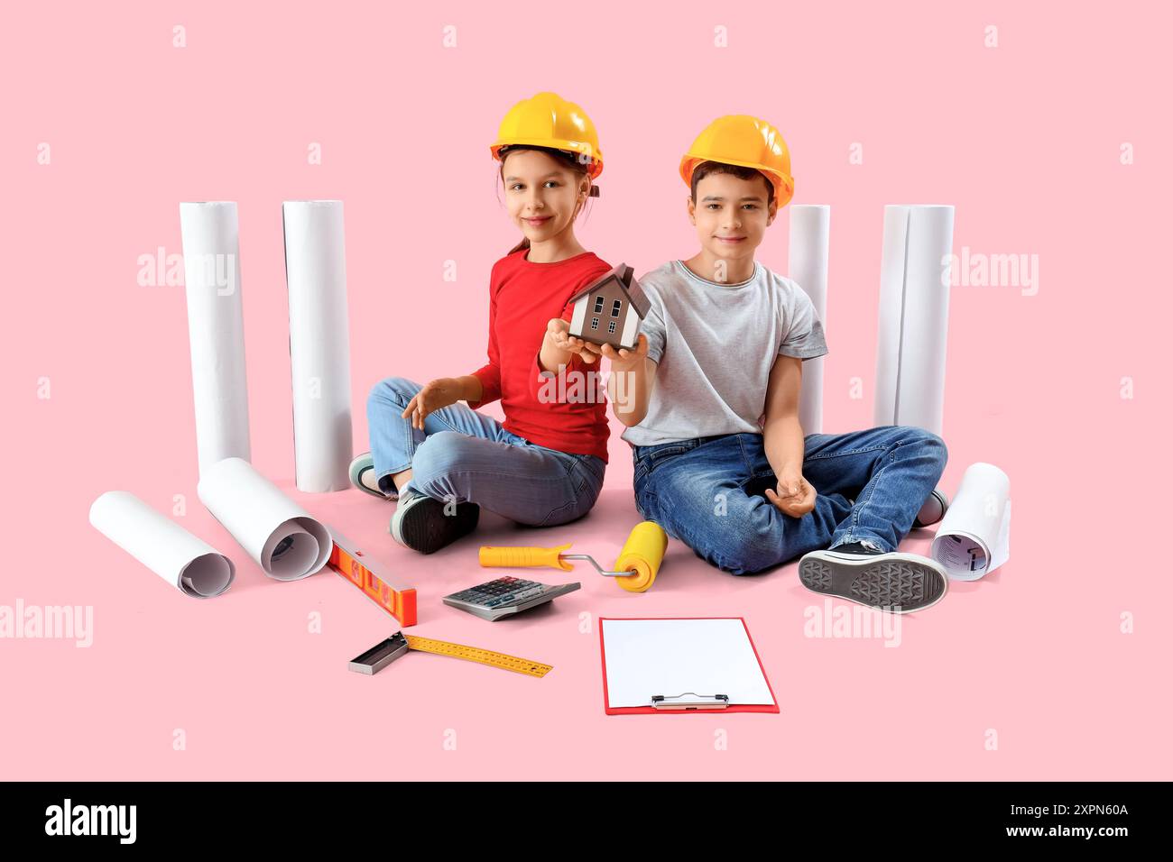 Little architects with house model and supplies sitting on pink ...