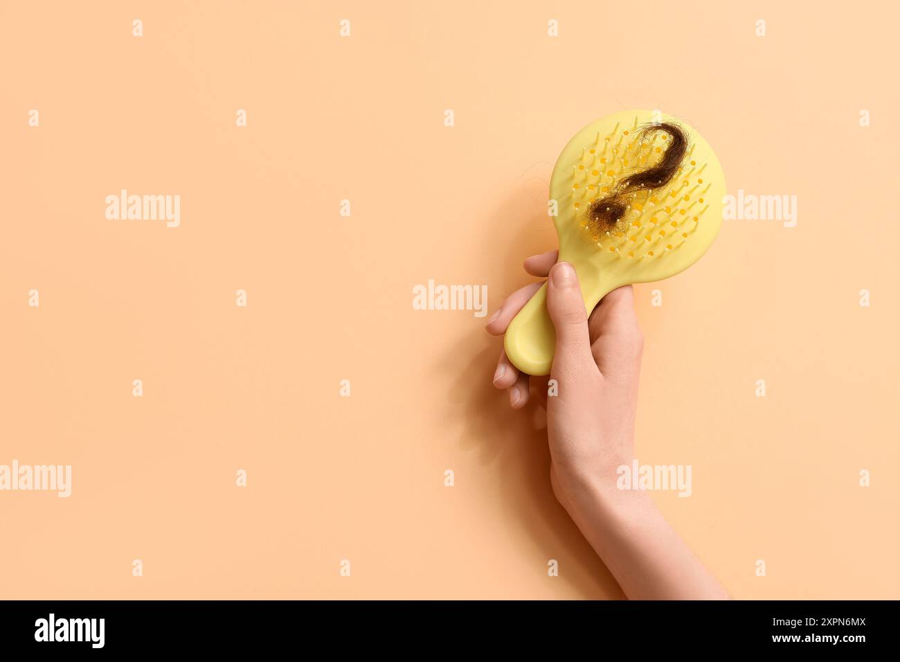 Hand with brush and clump of hair in shape of question mark on beige ...