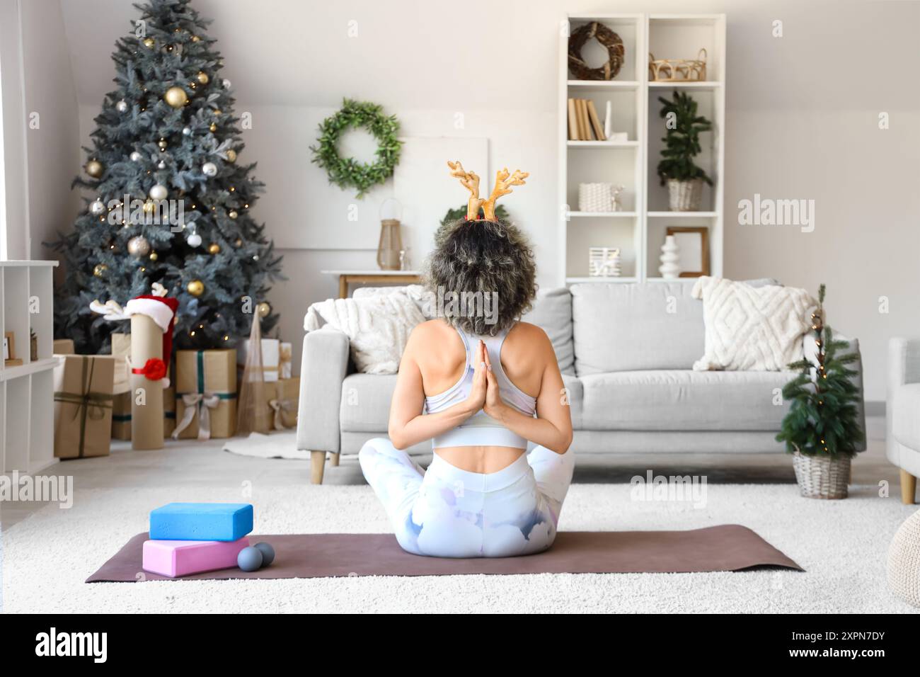 Sporty mature woman in reindeer horns doing yoga at home on Christmas ...