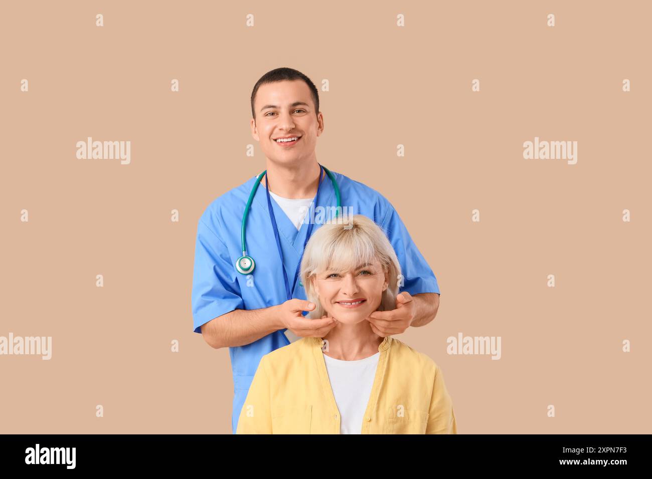 Male endocrinologist examining thyroid gland of mature woman on beige ...