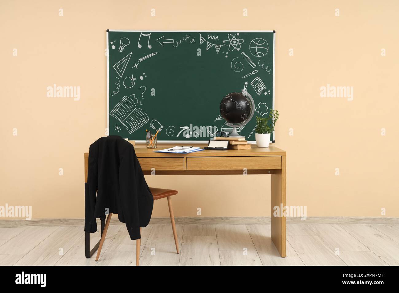 Teacher's table with school stationery and blackboard on beige wall in ...