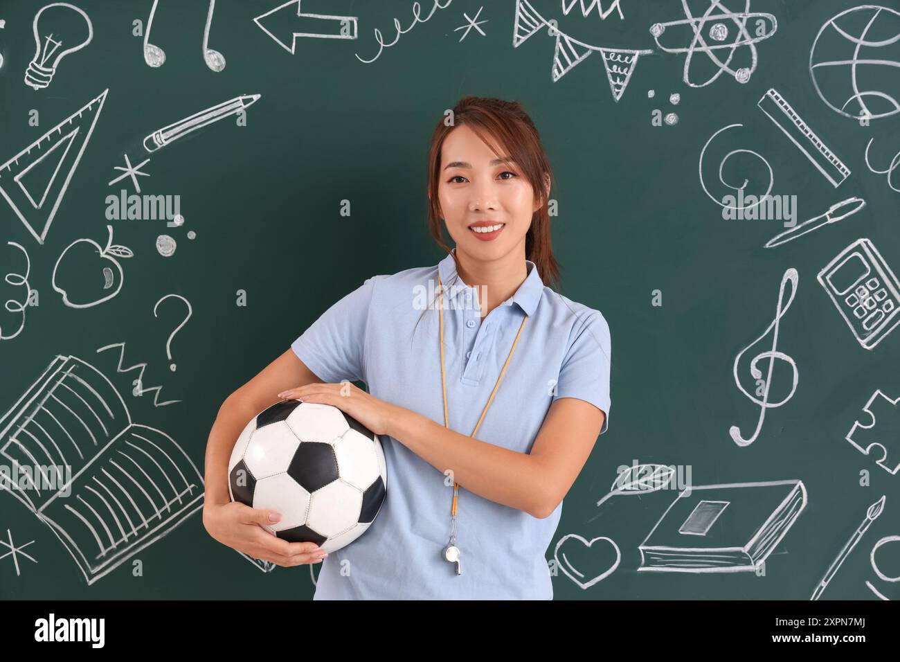 Female Asian PE teacher with soccer ball near blackboard in classroom ...