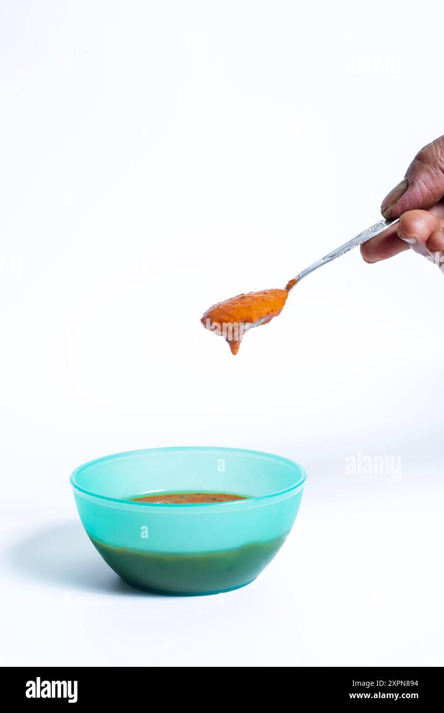 Onion chutney dripping from a spoon into a bowl on a white background ...