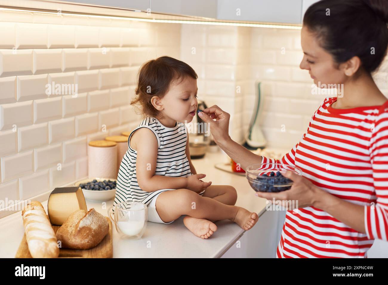 Little baby girl with her mother eating fresh blueberries in white ...