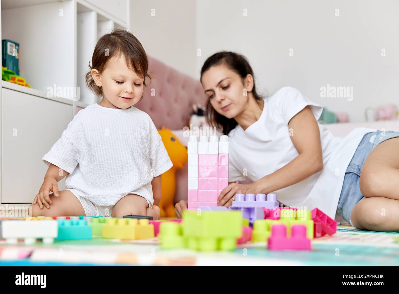 cute baby girl and her loving mother build tower from colorful cubes ...