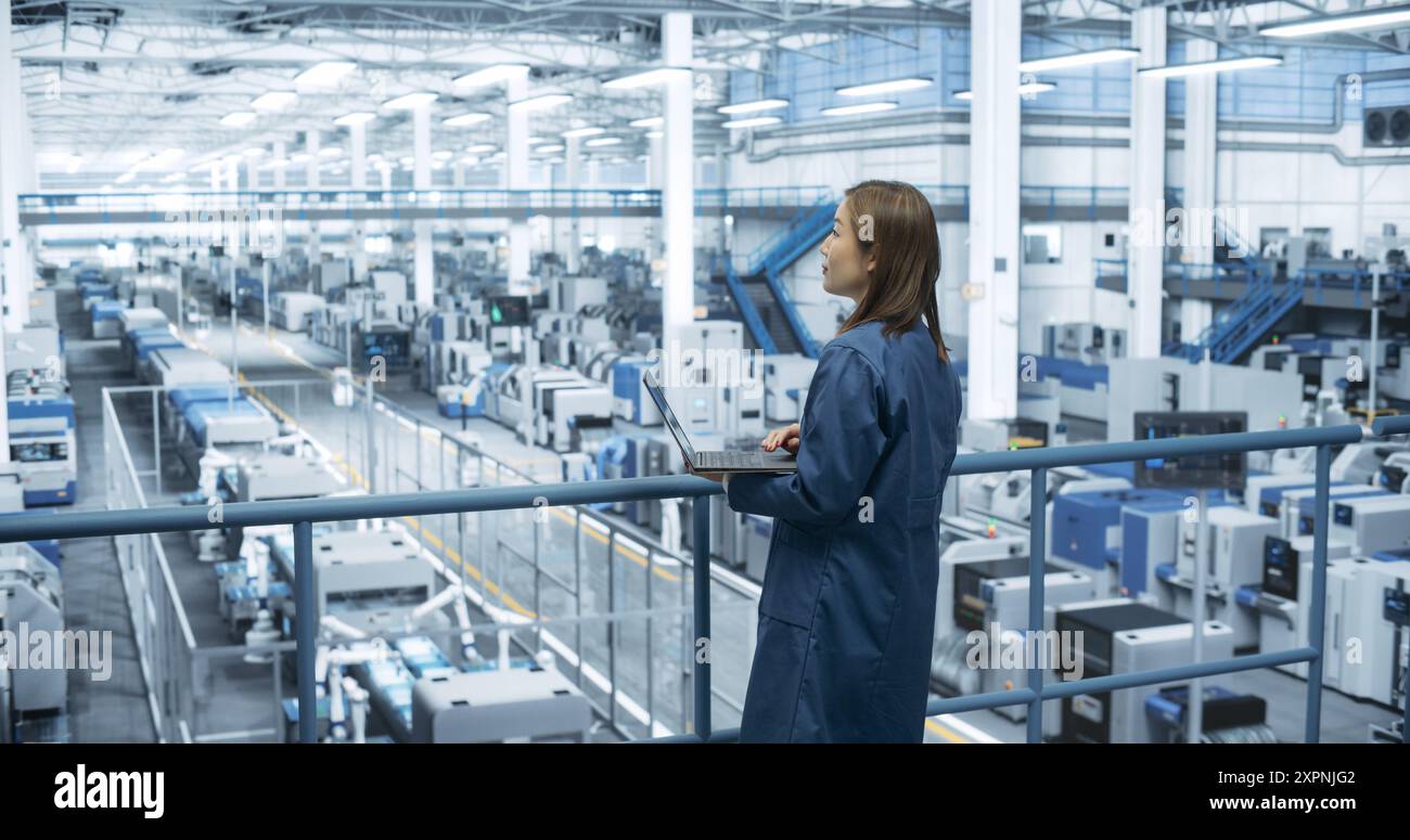 Japanese Factory Manager Working on Laptop at a Futuristic Industrial ...