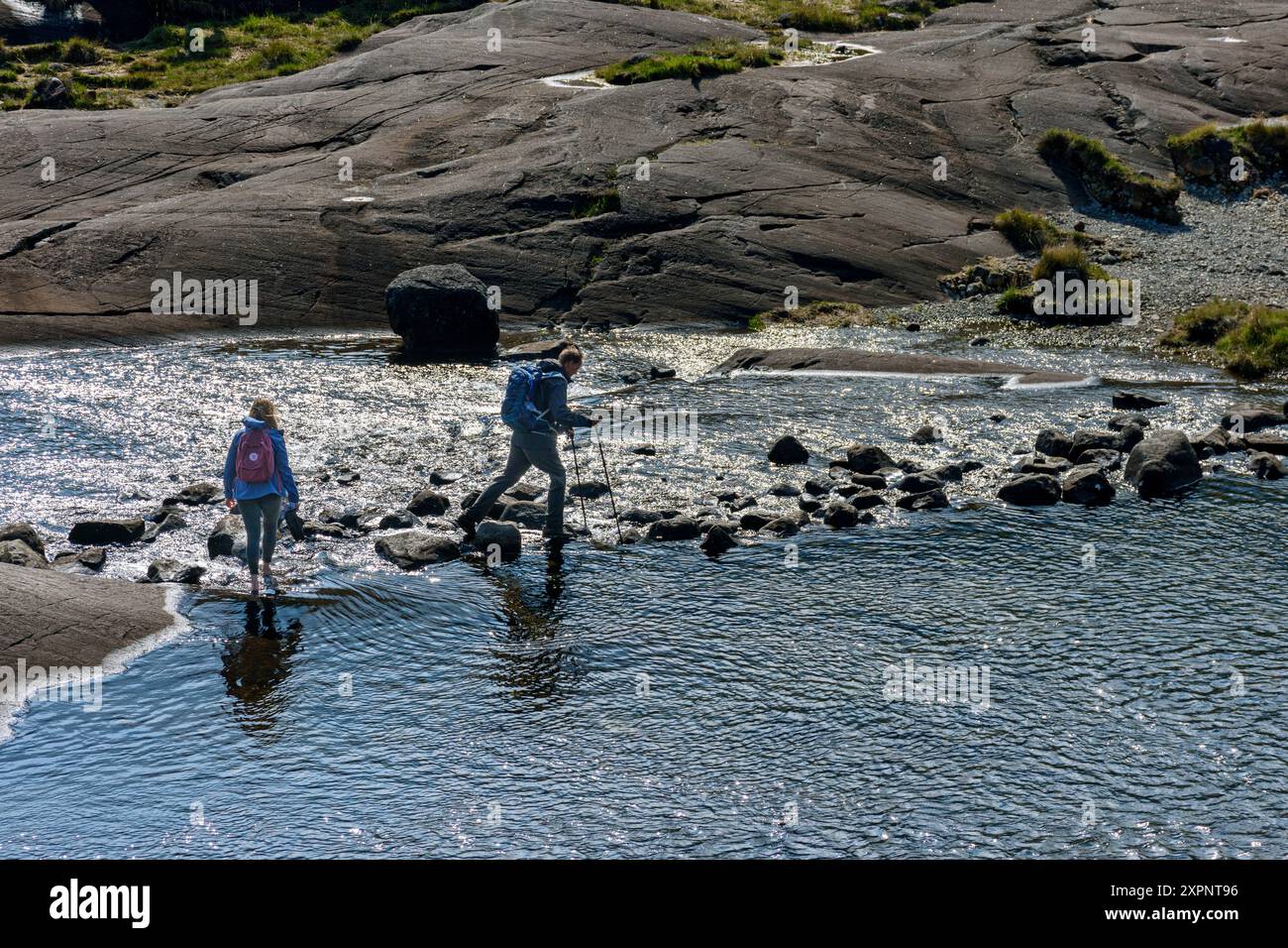 Two walkers crossing the stepping stones over the Scavaig river near ...