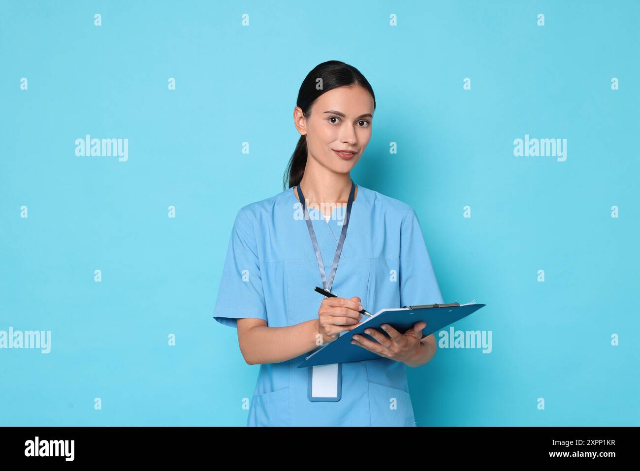 Beautiful nurse with clipboard writing notes on light blue background ...