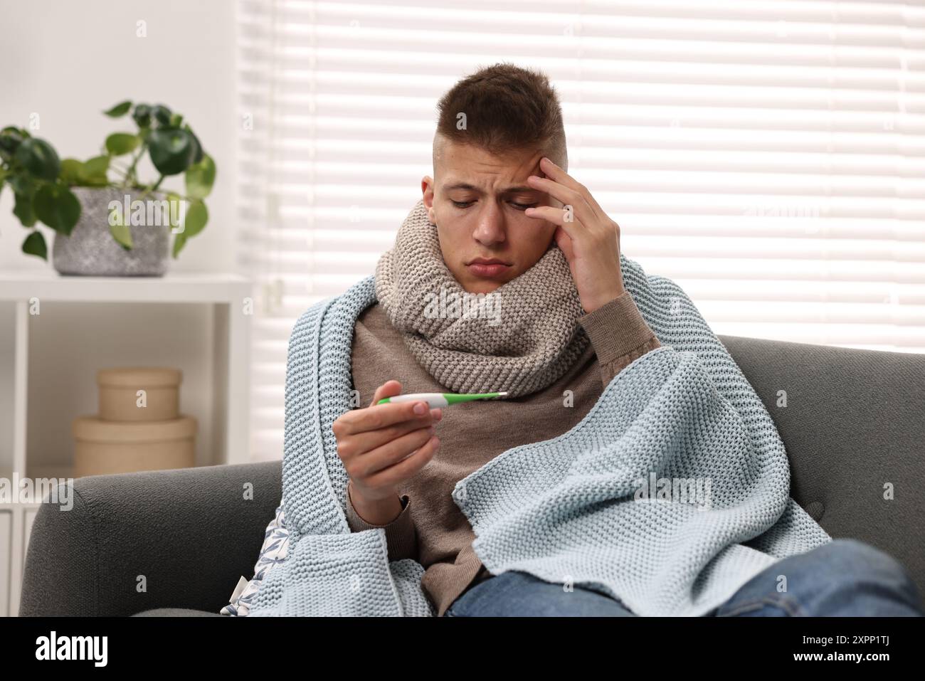 Cold symptom. Young man checking temperature with thermometer at home ...