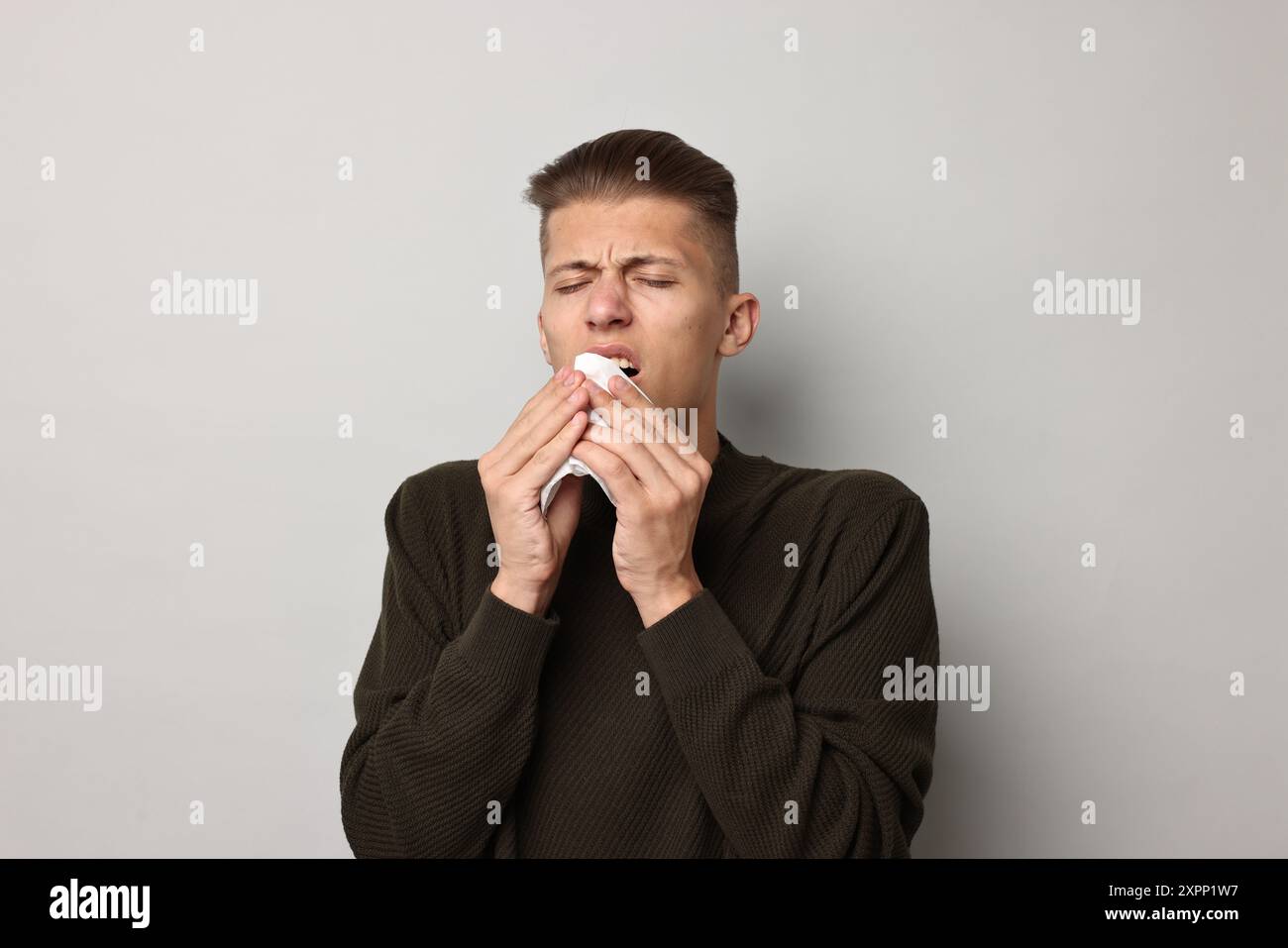 Sick man with tissue suffering from cold symptoms on light grey ...