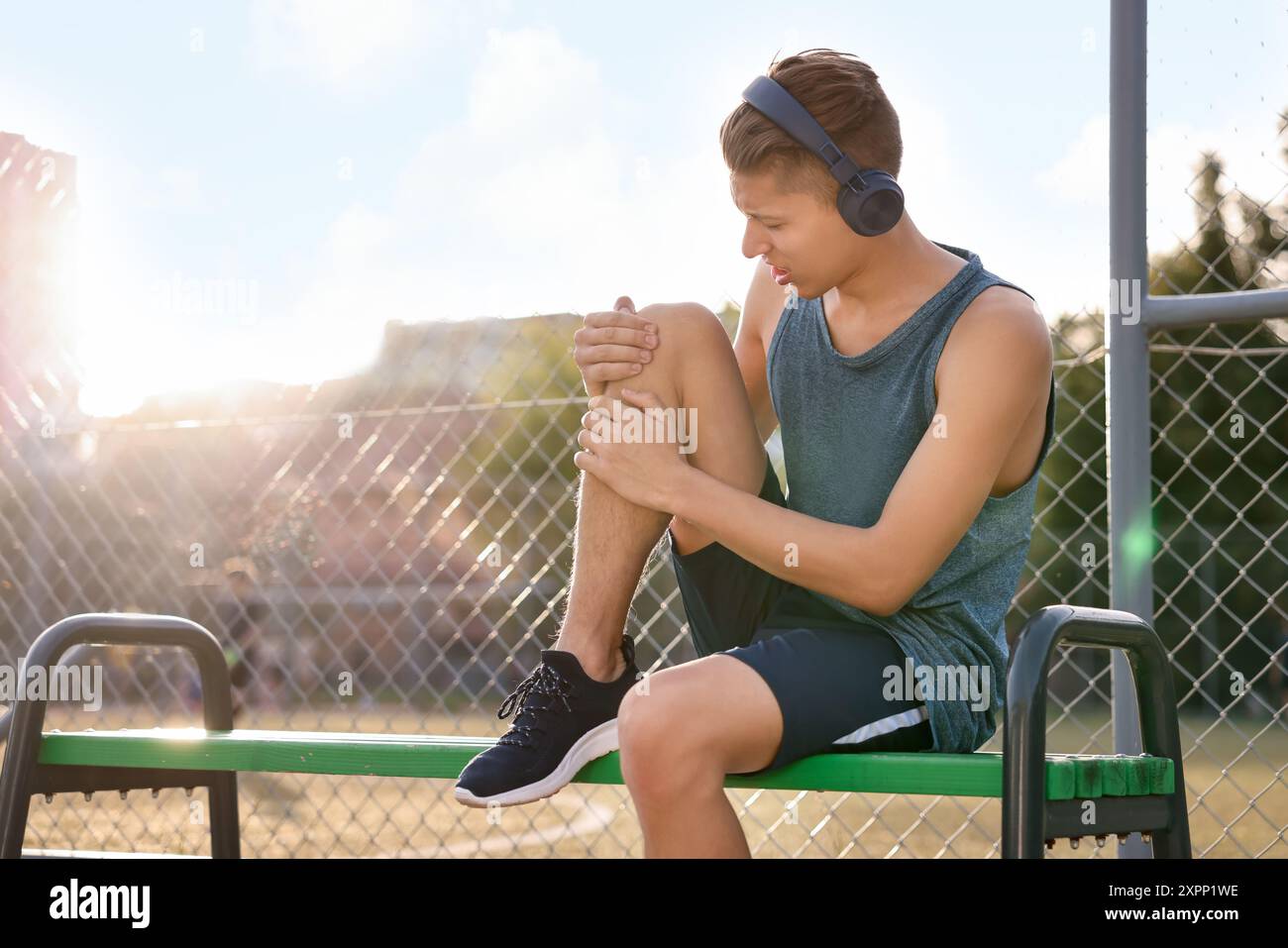 Sportsman with leg injury suffering from knee pain on bench at stadium ...